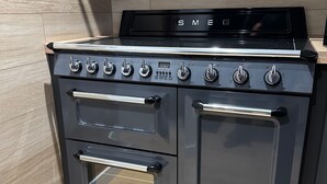 Cozinha moderna com fogão preto, forno de aço inoxidável e piso de madeira.