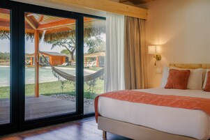 Quarto com uma cama grande, vista para a piscina e área externa, e porta de correr de vidro.