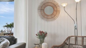 Quarto com cadeira de vime, espelho redondo e pequena mesa com velas e flores.
