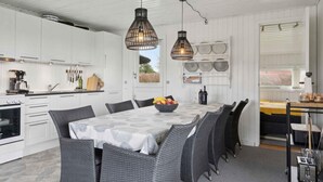 Cozinha moderna com armários brancos, mesa de jantar com toalha de mesa estampada, cadeiras de vime e luminárias pendentes.