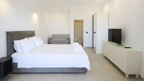 Quarto de hotel moderno com uma cama grande, um sofá, uma TV e um closet espaçoso.