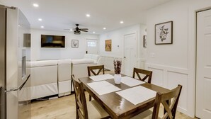 Uma sala de estar moderna com uma mesa de jantar, sofás brancos e uma televisão de tela plana na parede.