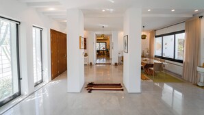Um corredor espaçoso com um tapete central, portas de madeira e uma área de jantar com mesa e cadeiras.