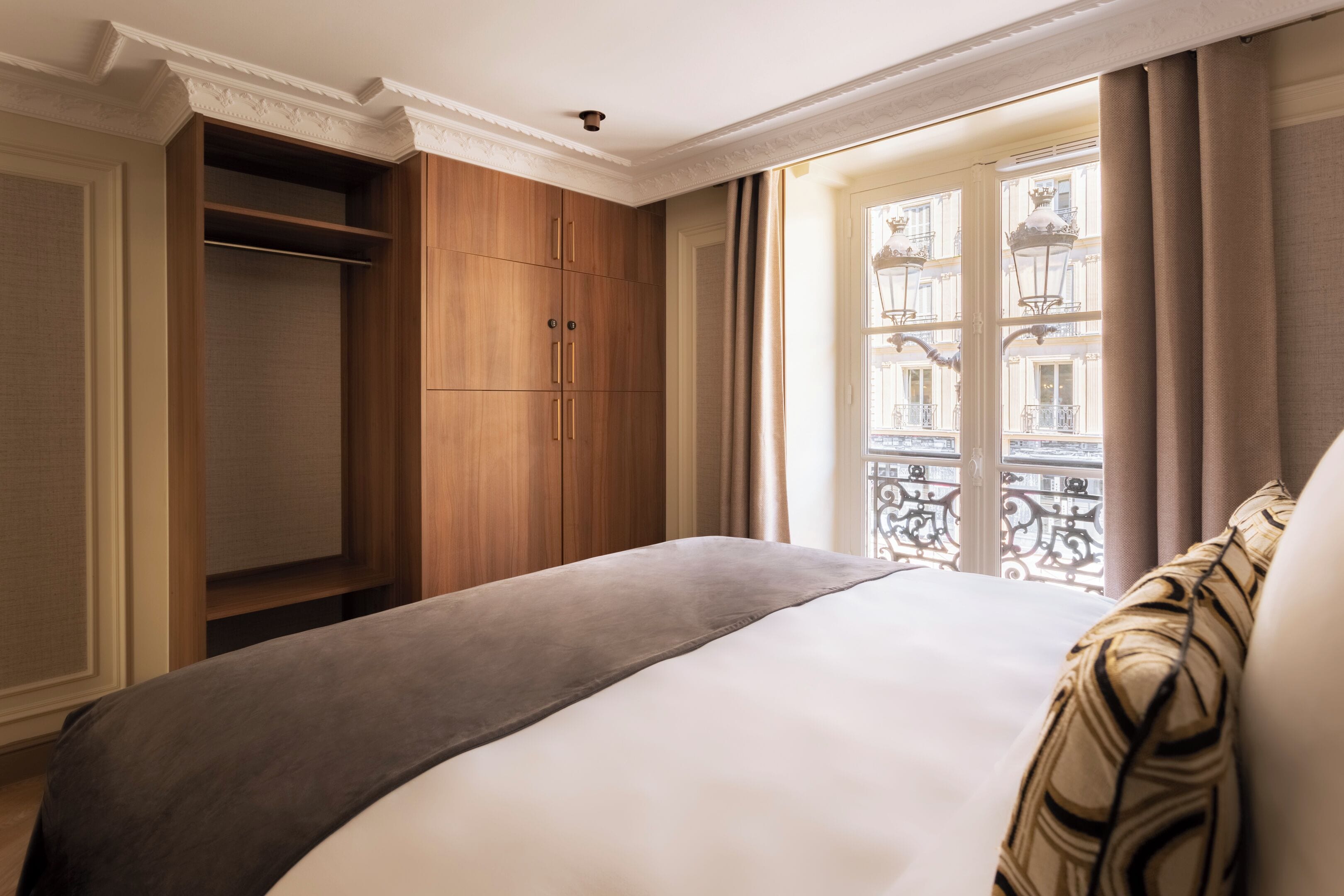 Quarto de hotel com cama, guarda-roupa e janela com vista para edifícios.