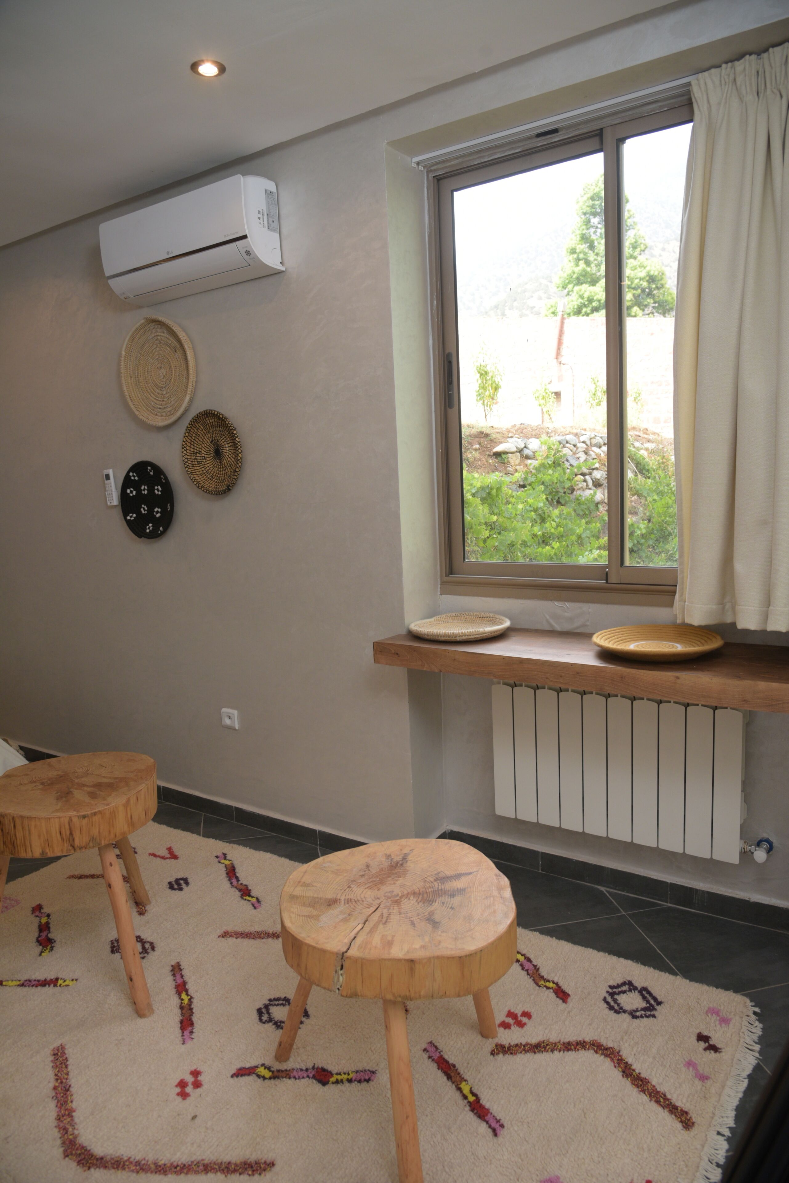 Quarto com janela, radiador, cesta de palha, banquinho de palha e tapete estampado.