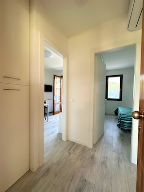 Um corredor com piso de madeira que leva a um quarto com cama e janela.