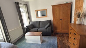 Um quarto com um sofá cinzento, um armário de madeira, uma pequena mesa branca e um espelho na parede.