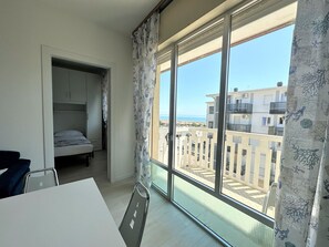 Varanda com vista para o mar e edifícios, uma cama, uma mesa e uma cadeira.