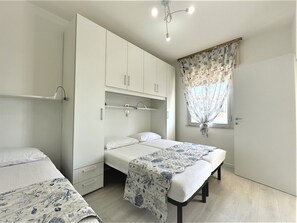 Quarto com cama, guarda-roupa, mesa de cabeceira e janela com cortinas.