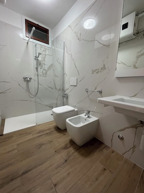 Uma casa de banho moderna com chuveiro, sanita, bidé e lavatório.