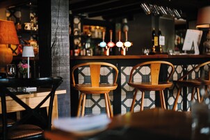 Uma área de bar com cadeiras de madeira, balcão e uma luminária.