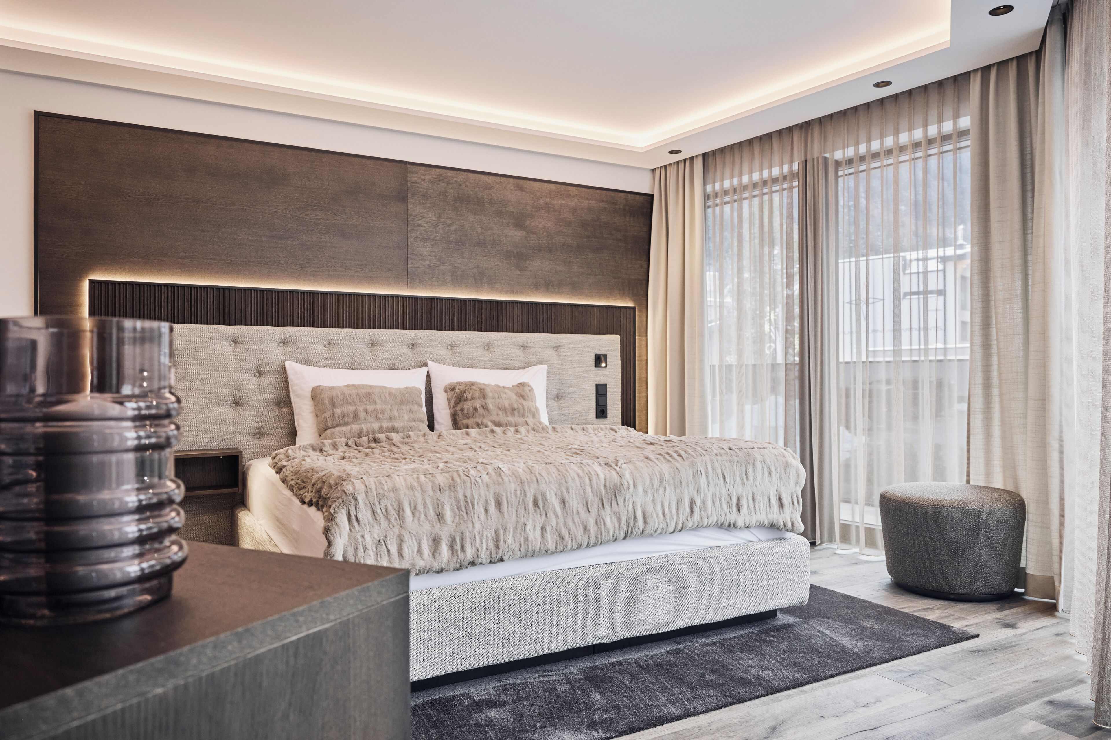 Quarto moderno com uma cama grande, mesa de cabeceira e uma janela ampla com cortinas.