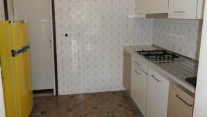 Uma cozinha compacta com geladeira amarela, paredes com azulejos brancos, fogão a gás e pia.