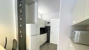 Uma cozinha compacta com eletrodomésticos brancos, painel de parede escuro e uma porta que dá para outro cômodo.