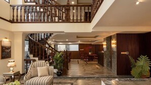 Um hall espaçoso com uma escadaria imponente, uma área de estar com um sofá estampado e um balcão de recepção.