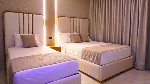 Quarto de hotel com duas camas, uma mesa de cabeceira e uma janela grande com cortinas.