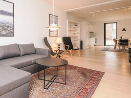 Uma sala de estar moderna com um sofá cinzento, uma mesa de centro redonda e tapetes estampados.