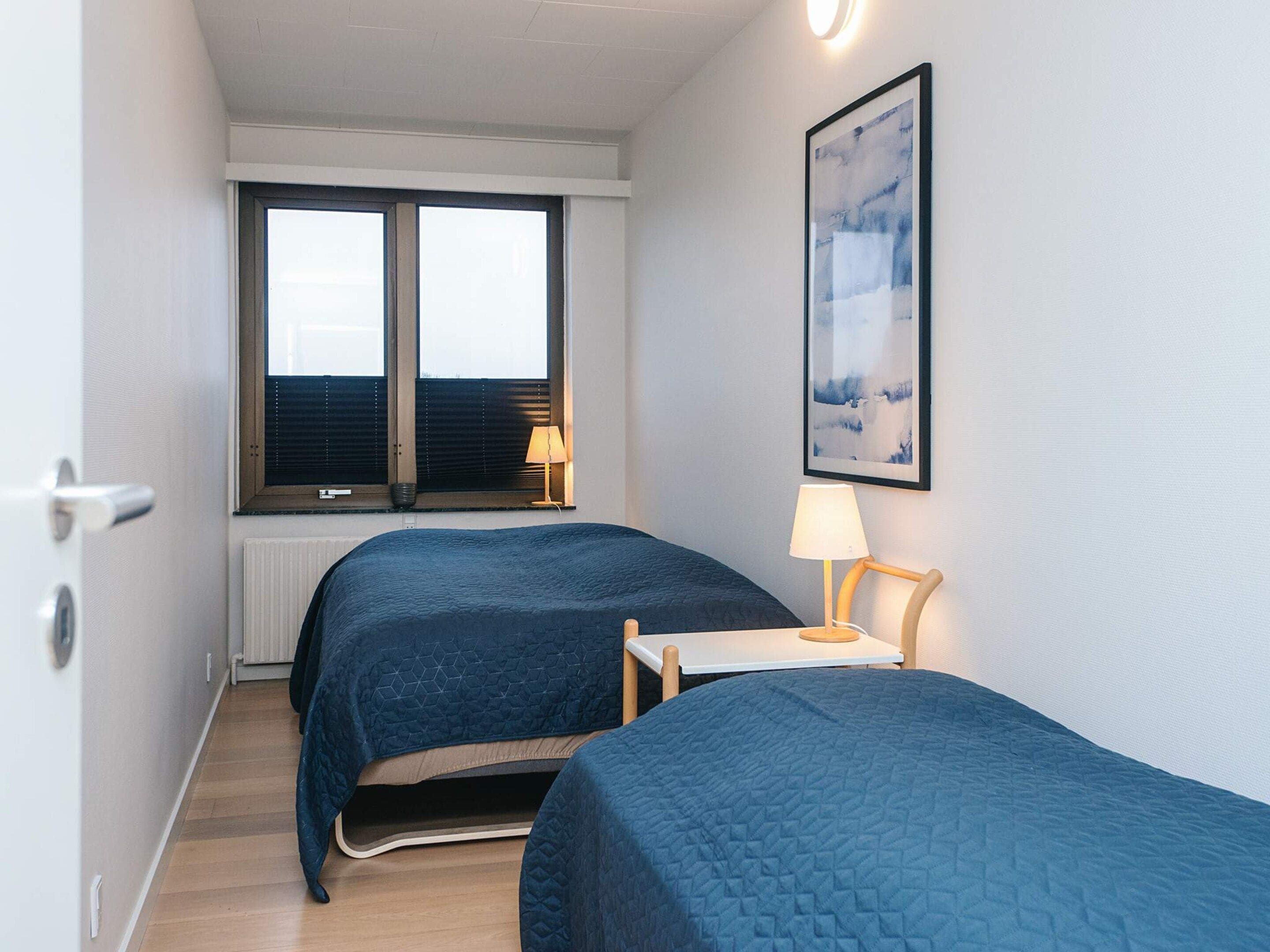 Quarto de hotel com duas camas, janela com persianas, quadro na parede e pequena mesa com abajur.