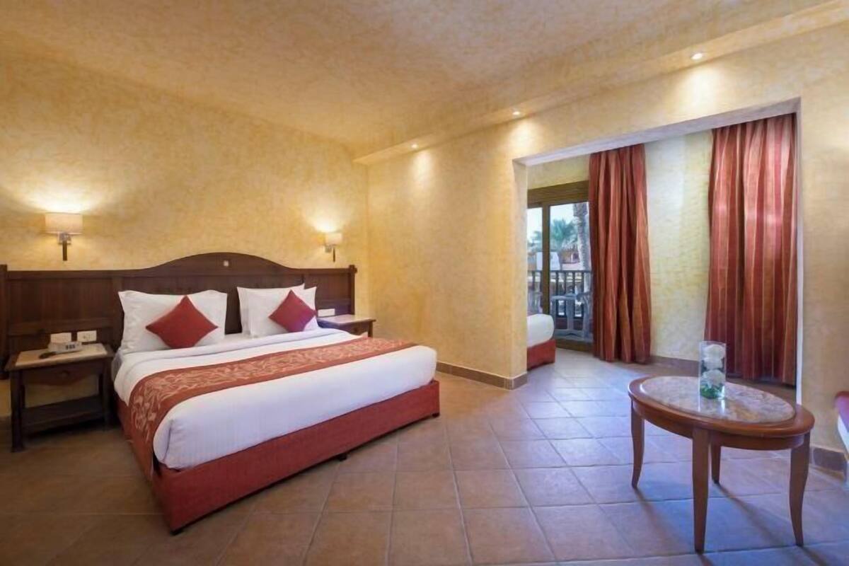 Quarto de hotel com uma cama, mesas de cabeceira, uma mesa redonda e vista para o exterior.