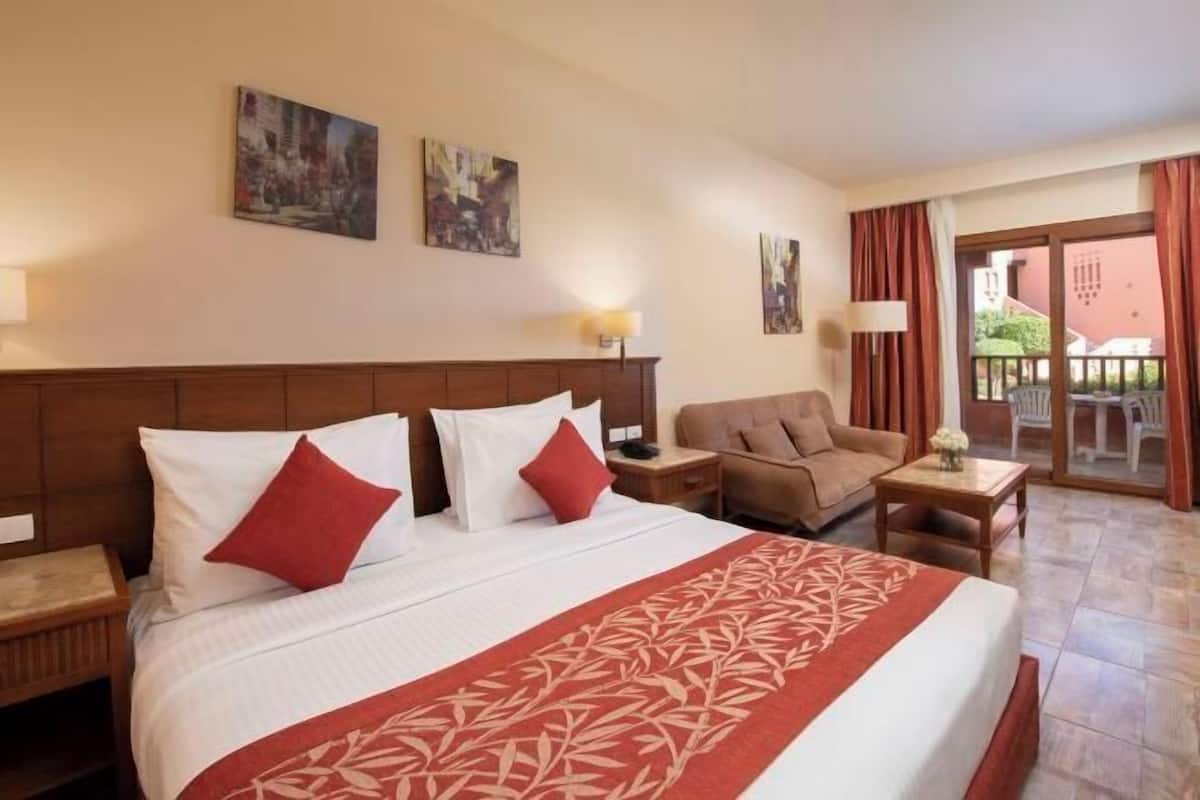 Quarto de hotel com uma cama grande, um sofá, uma mesinha e varanda com cortinas.