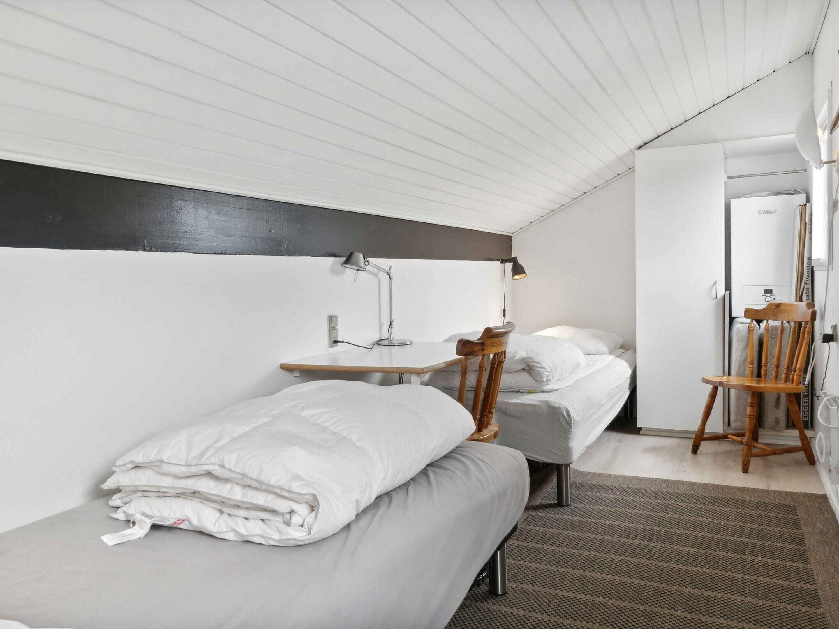 Quarto de hotel compacto com duas camas, uma escrivaninha e uma cadeira.