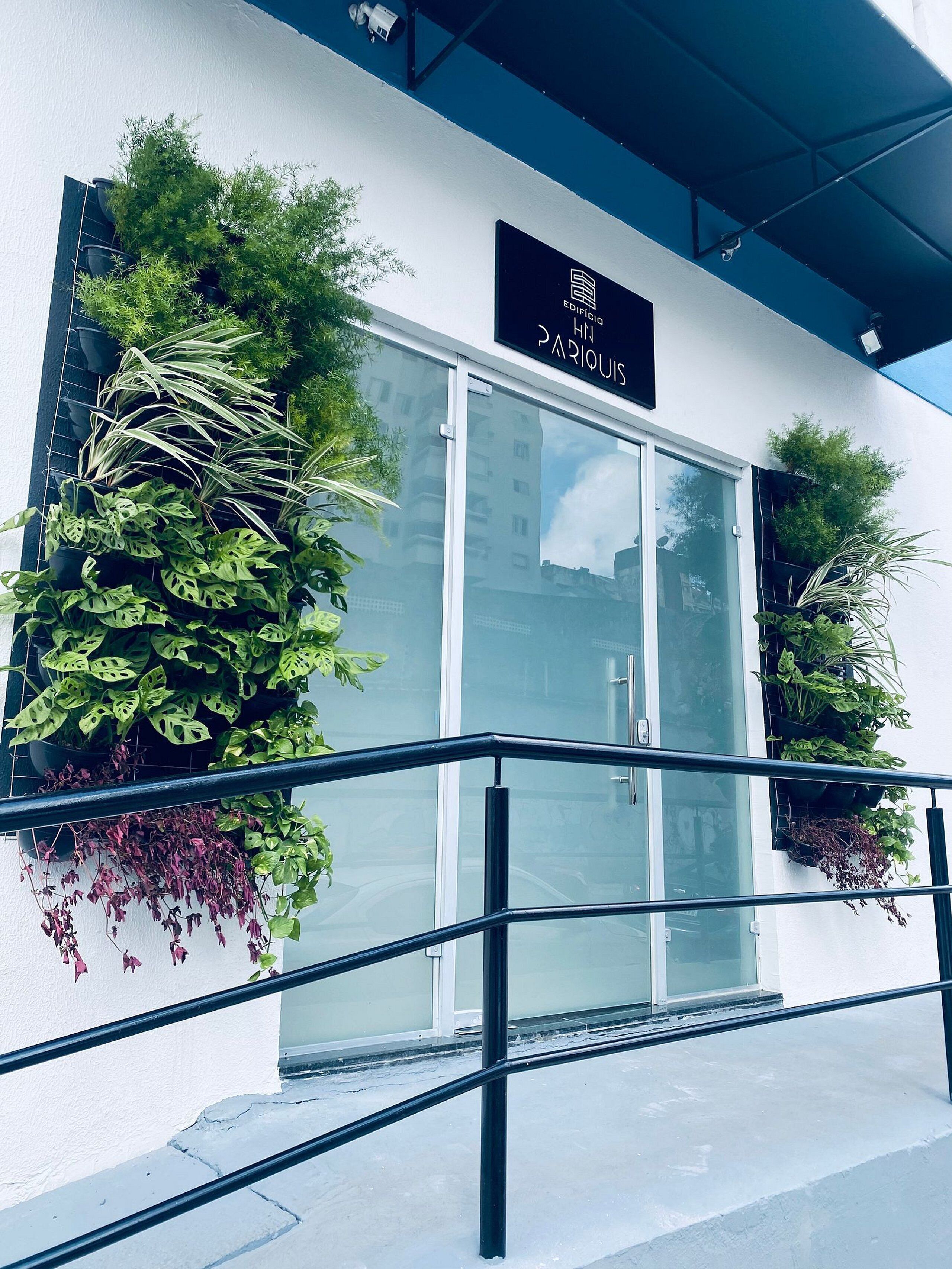 Entrada de hotel com porta de vidro, plantas em vasos de cada lado e um letreiro acima da porta.