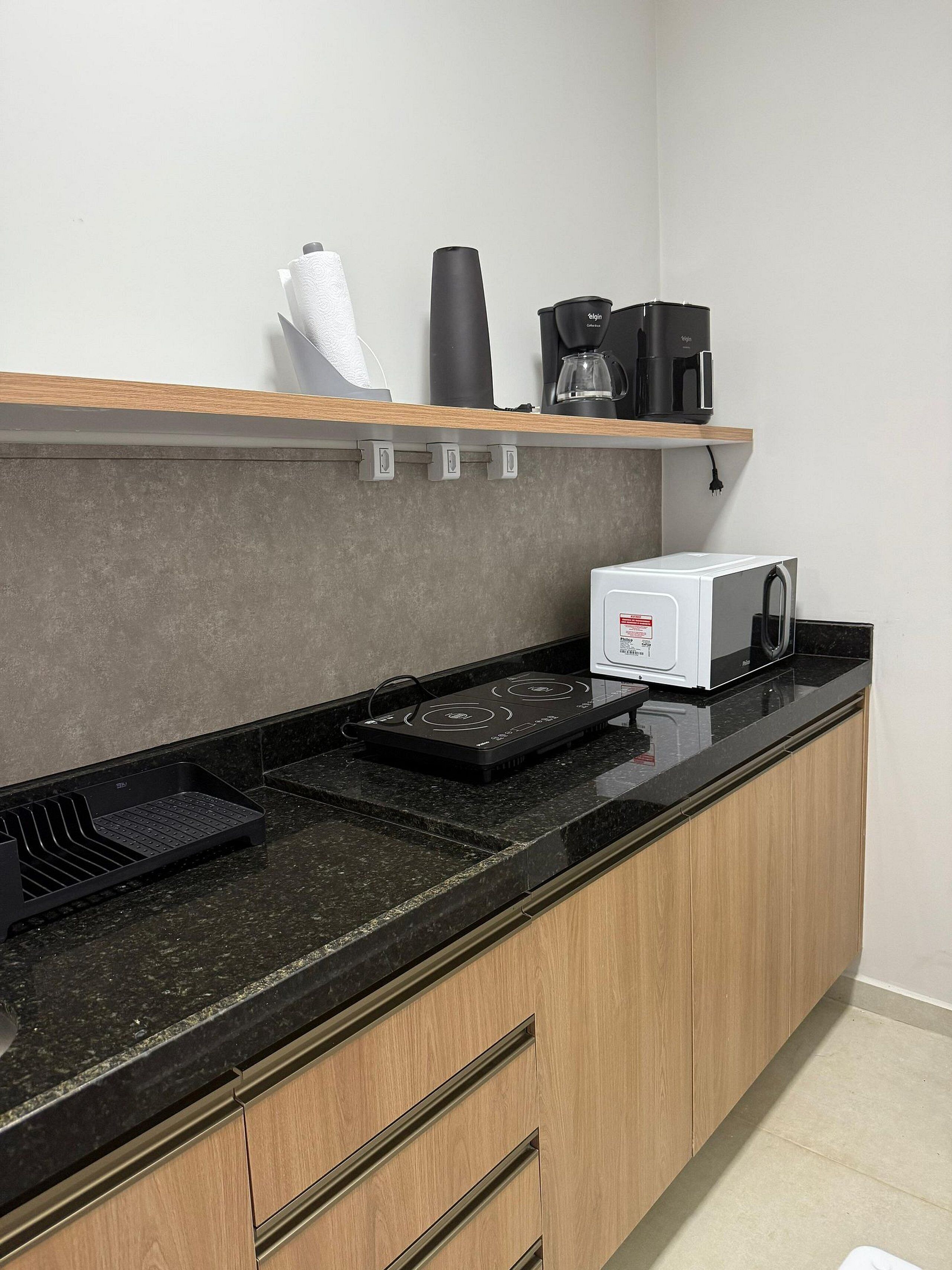 Uma cozinha moderna com bancada preta, cafeteira, micro-ondas e torradeira.