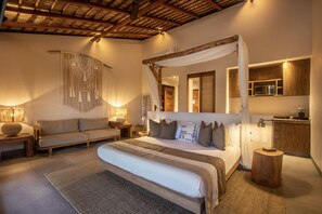 Um quarto espaçoso com uma cama grande, um dossel, um espaço de estar com um sofá e uma cozinha compacta.