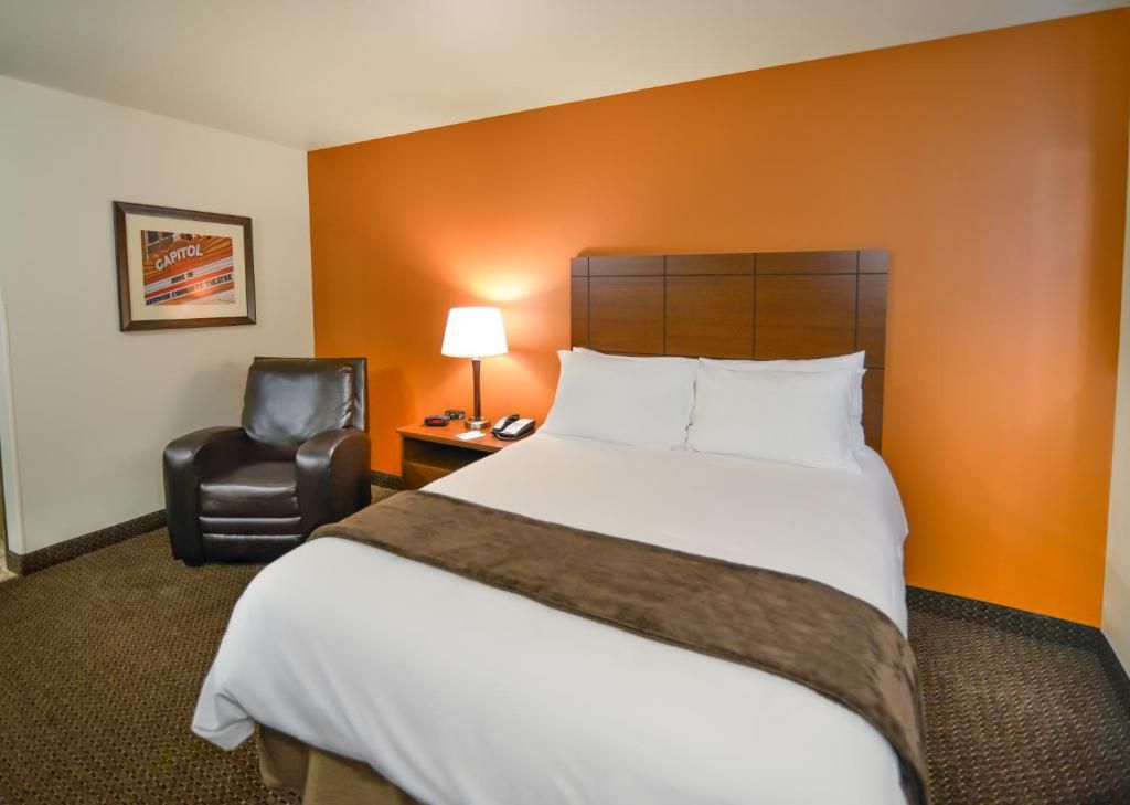 Quarto de hotel com uma cama grande, uma cadeira, uma mesa de cabeceira com abajur e um quadro pendurado na parede.