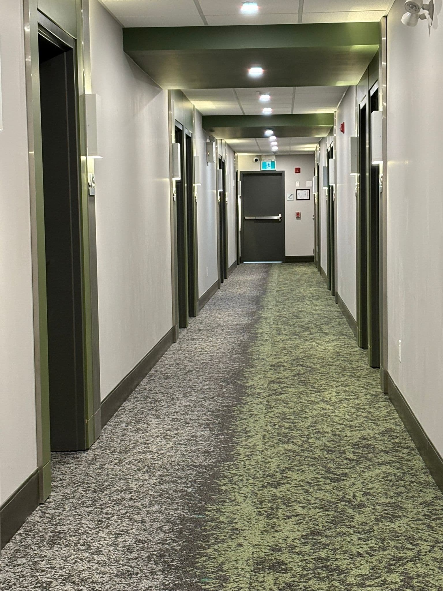Um corredor comprido e estreito, com piso coberto por carpete e portas em ambos os lados.