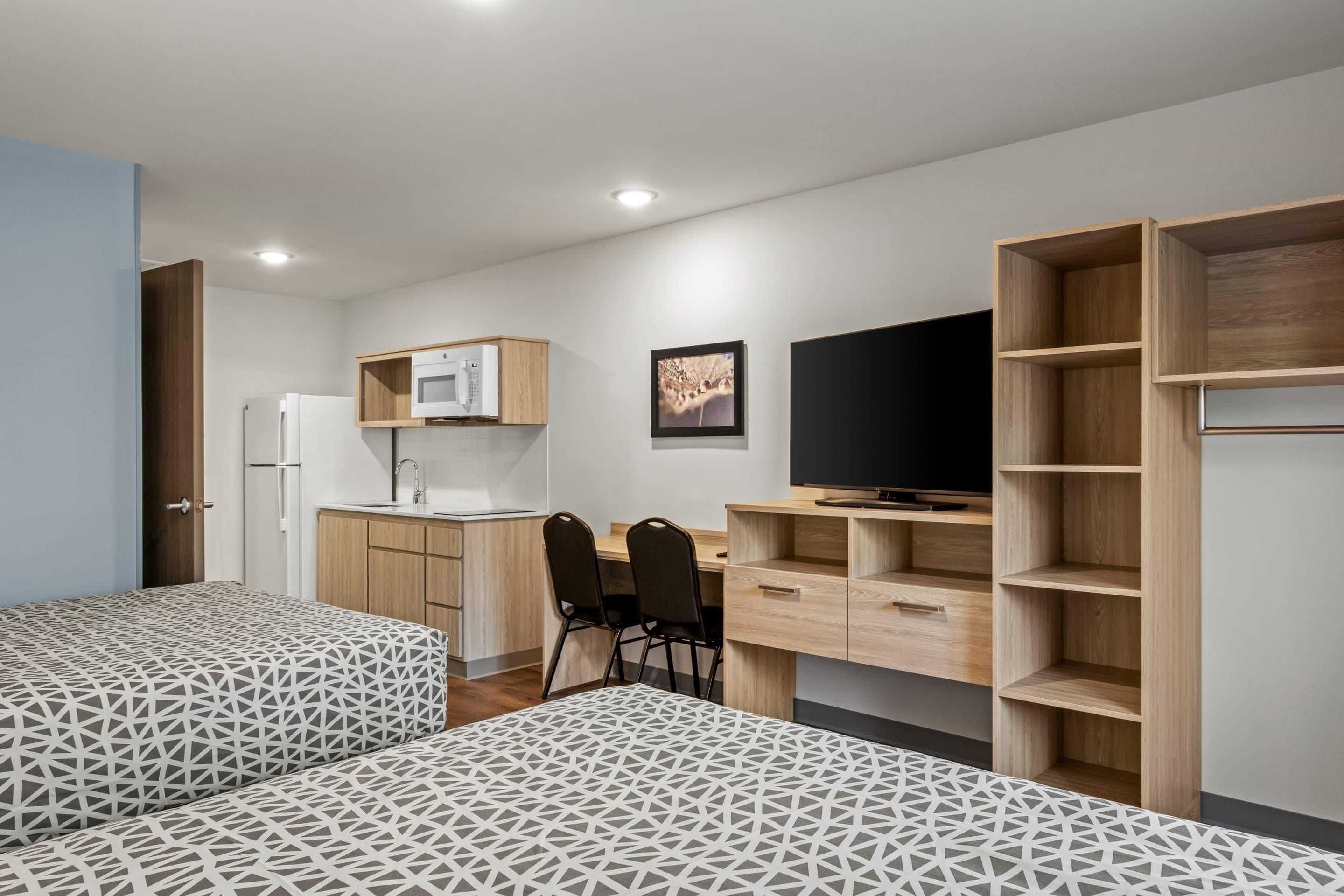 Quarto compacto com duas camas, cozinha compacta, área de refeições e televisão.