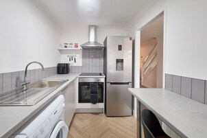 Uma cozinha compacta com pia de aço inoxidável, forno embutido, geladeira e máquina de lavar.