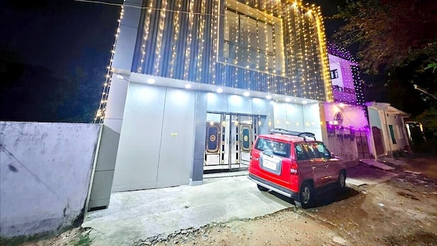 Um edifício moderno com entrada de vidro, um carro vermelho estacionado na frente e luzes decorativas.