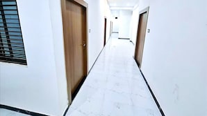 Um corredor comprido e estreito, com paredes brancas e chão de mármore.