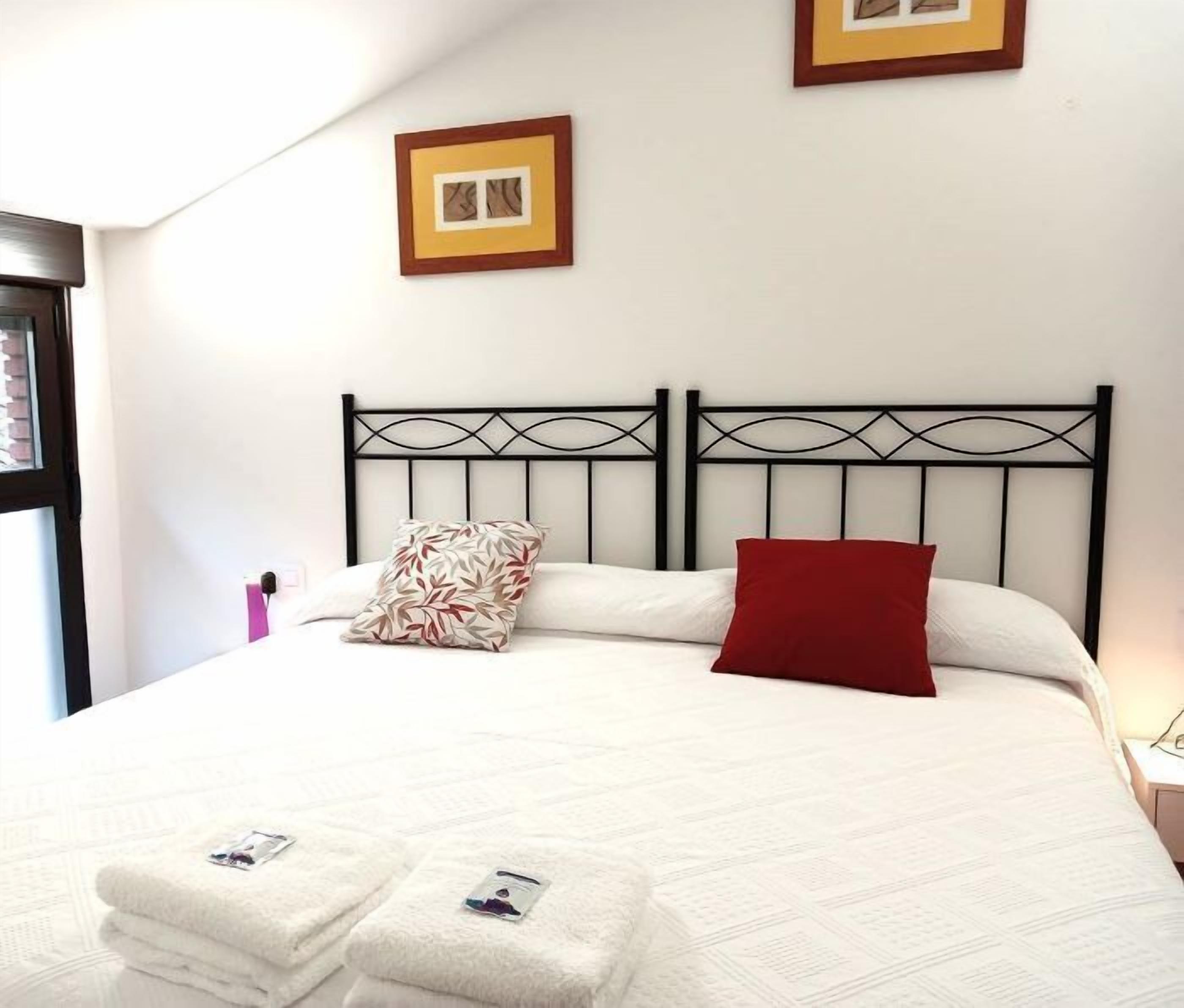 Cama bem arrumada com lençóis brancos, duas almofadas e toalhas dobradas.
