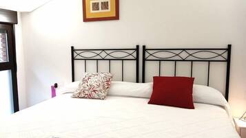 Cama bem arrumada com lençóis brancos, duas almofadas e toalhas dobradas.