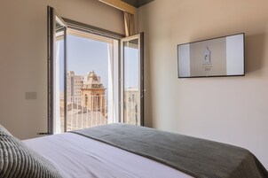 Quarto de hotel com uma cama, uma janela grande e um quadro na parede.