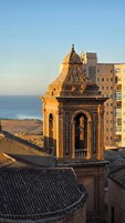 Um edifício histórico com cúpula e arcos, com vista para uma área costeira com edifícios modernos ao fundo.