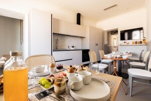Uma cozinha moderna com armários brancos, uma área de refeições com mesa posta para o café da manhã e uma janela grande que oferece luz natural.