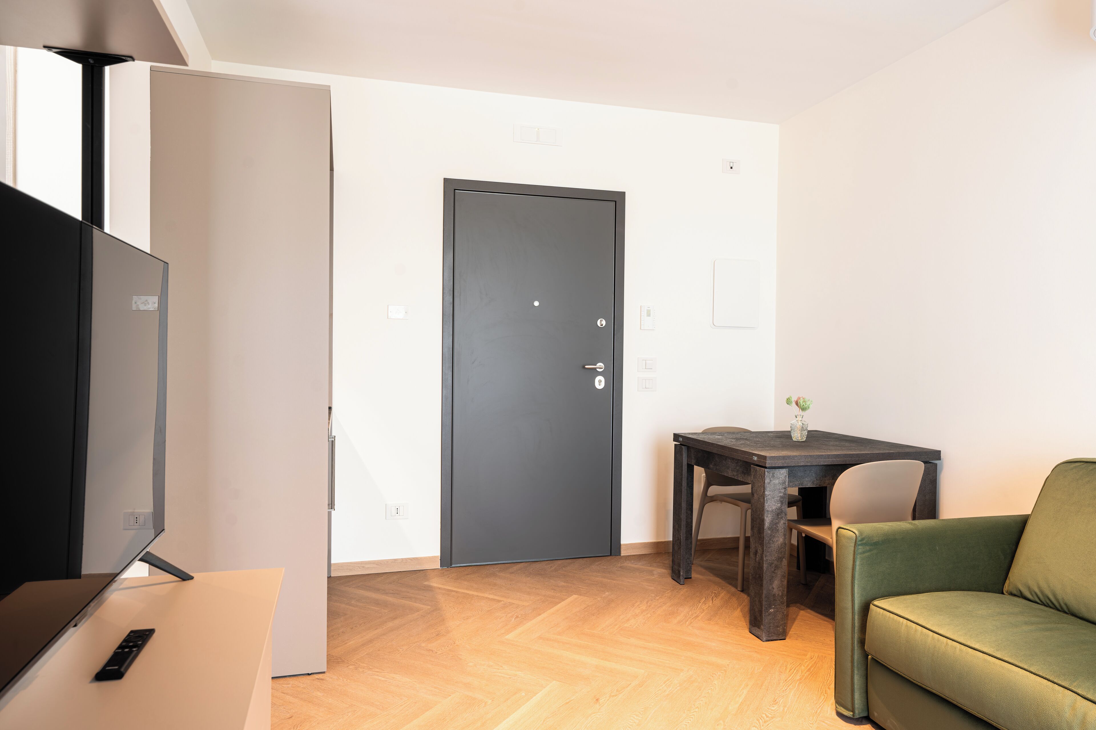 Uma sala de estar moderna com televisão de tela plana, sofá, mesa de jantar e uma porta.