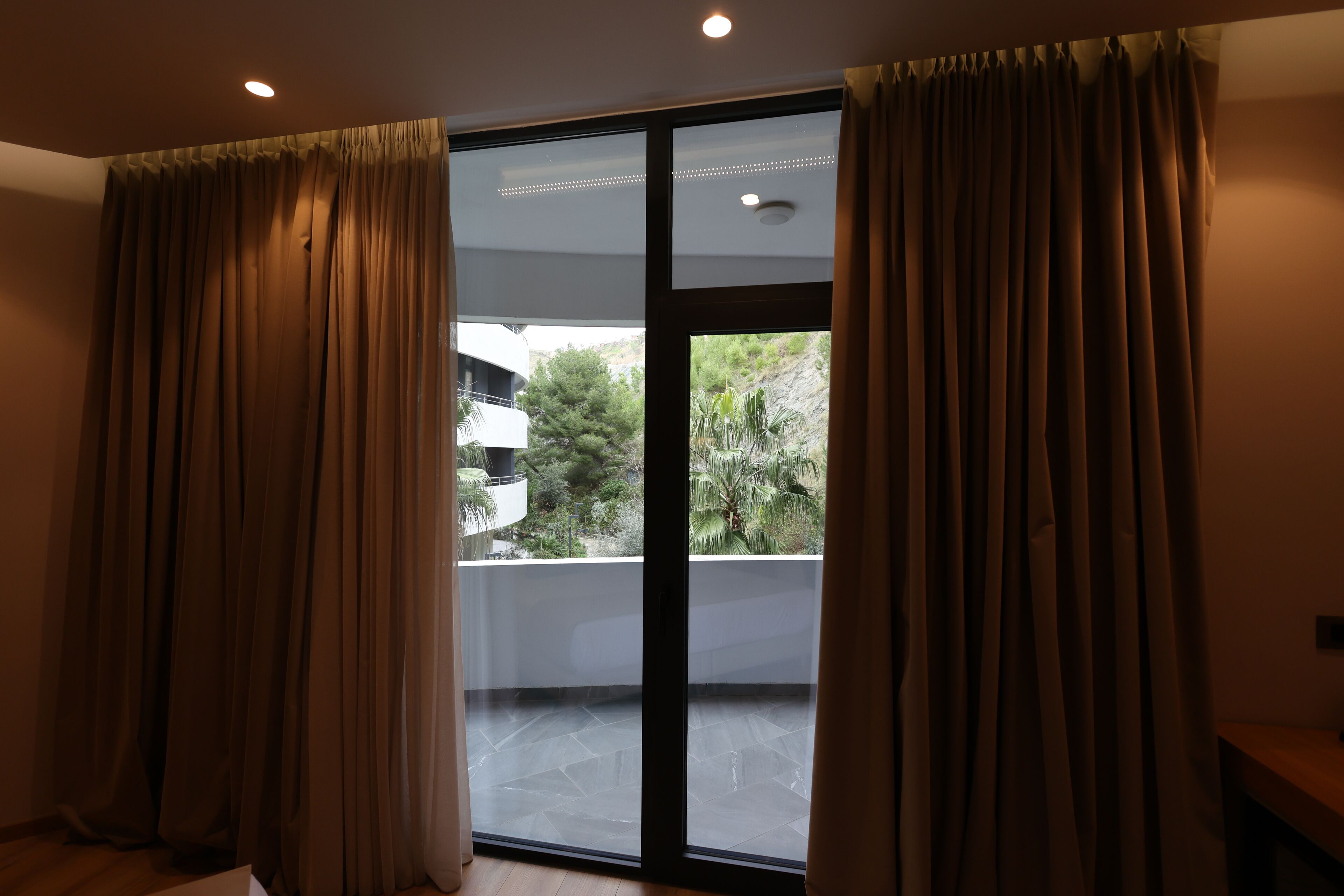 Quarto com porta de correr de vidro que dá para uma varanda com vista para áreas verdes e edifícios.