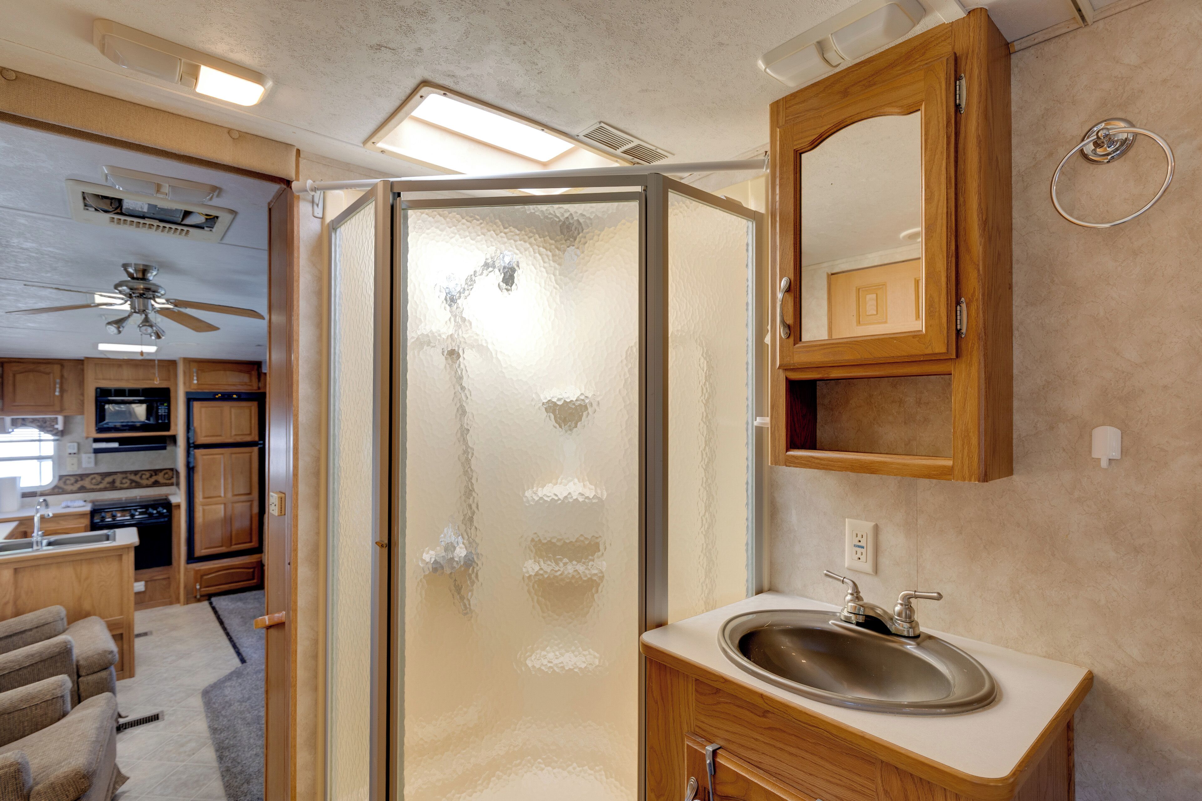 Casa de banho compacta numa RV, com cabine de duche em vidro, lavatório e espelho.