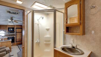 Casa de banho compacta numa RV, com cabine de duche em vidro, lavatório e espelho.