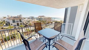 Varanda com mesa e cadeiras, oferecendo vista do oceano e edifícios próximos.