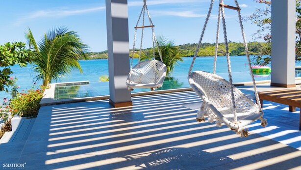 Um espaço ao ar livre tranquilo com dois balanços de vime branco, com vista para uma piscina e um céu azul claro.