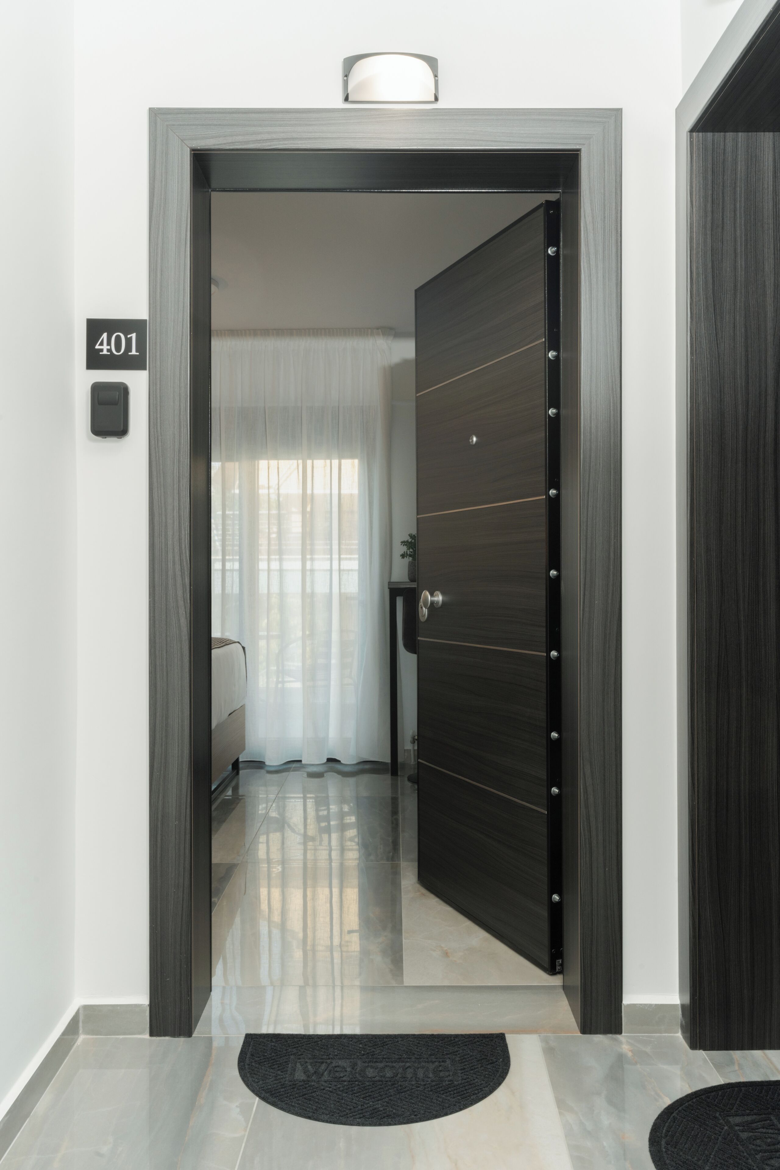 Entrada de hotel moderna com porta de madeira escura, tapete de boas-vindas e placa indicando a sala 401.