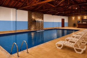 Piscina com muro de pedra e cascata, rodeada por espreguiçadeiras.