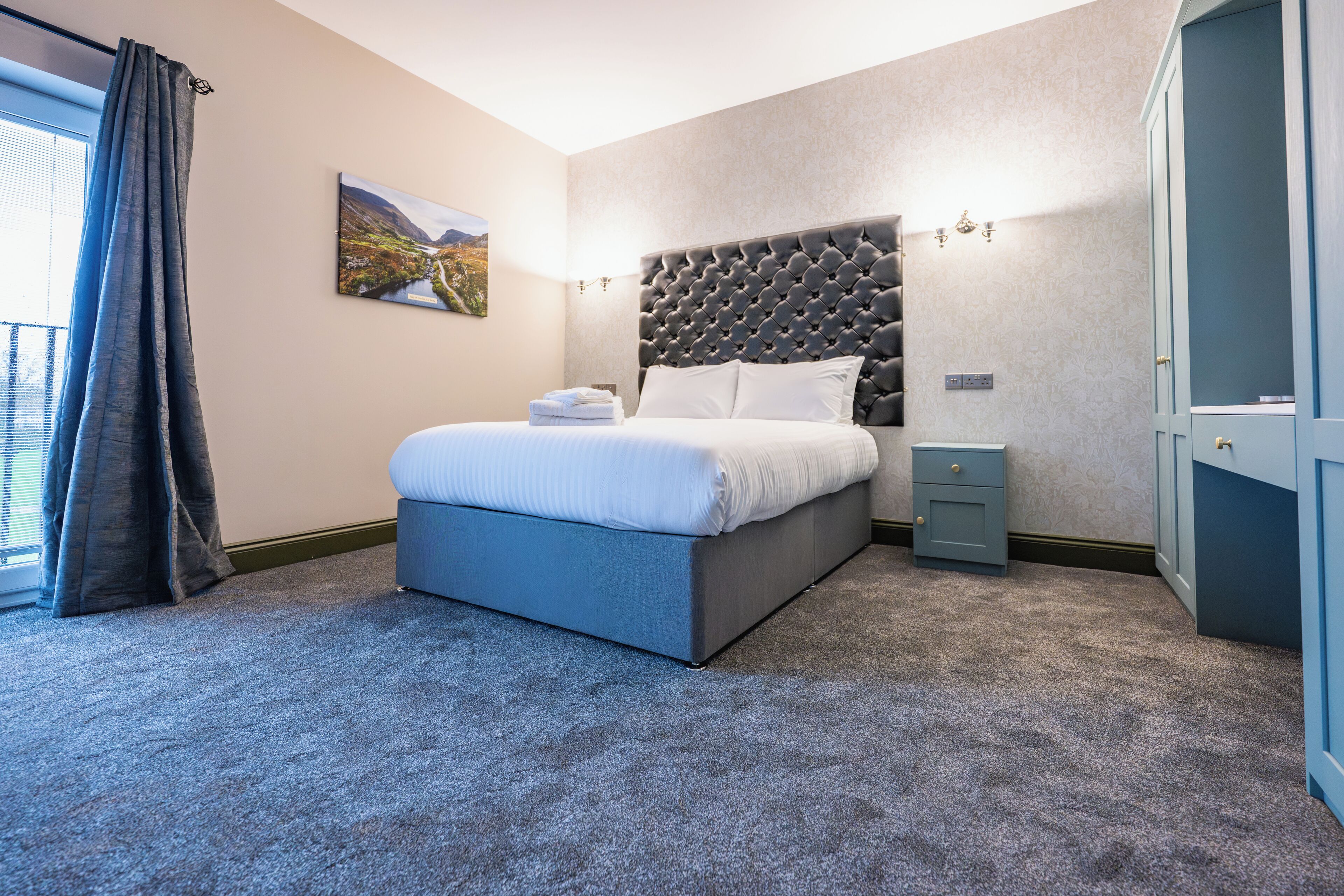 Quarto de hotel moderno com uma cama grande, uma mesa de cabeceira, um guarda-roupa e um quadro na parede.