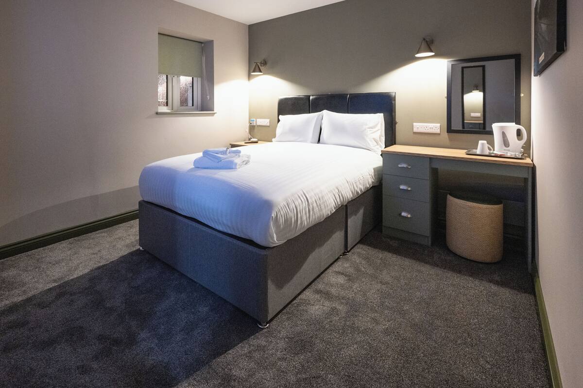 Quarto de hotel moderno com uma cama grande, uma escrivaninha e uma janela pequena.