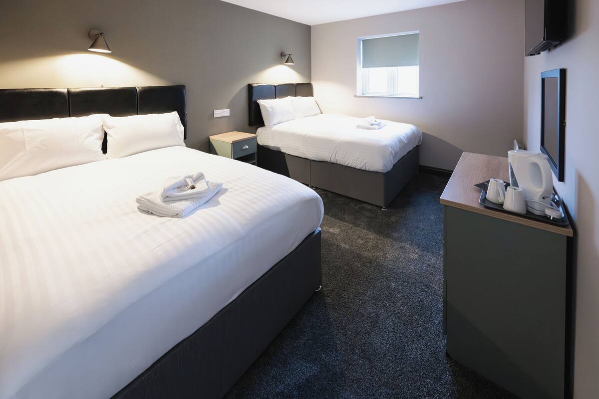 Quarto de hotel com duas camas, uma escrivaninha pequena com telefone e uma televisão na parede.